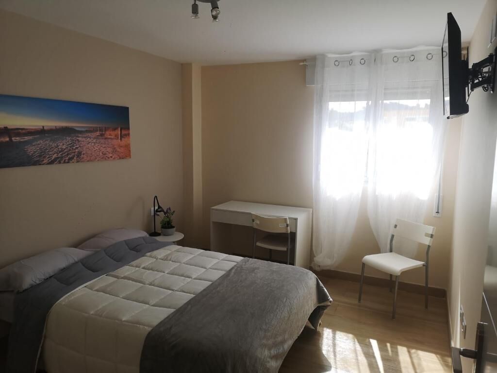 Quarto com cama, escrivaninha, cadeira e televisão.