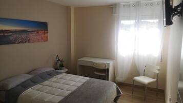 Quarto com cama, escrivaninha, cadeira e televisão.