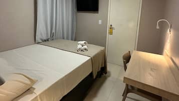 Quarto individual com uma mesa e cadeira de madeira, televisão de tela plana fixada na parede e uma porta com uma placa.