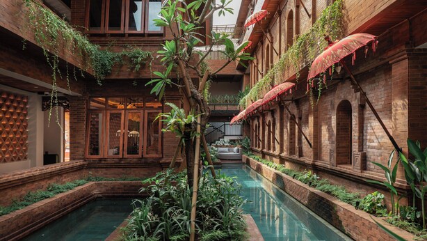 Um pátio com piscina central, paredes de tijolo e plantas pendentes.