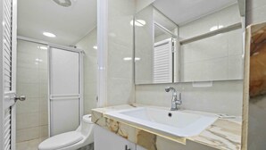 Um banheiro moderno com vaso sanitário branco, pia com bancada de mármore e um espelho grande.
