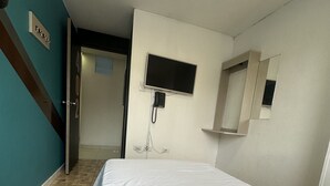 Quarto de hotel com cama, televisão presa na parede, telefone e espelho.