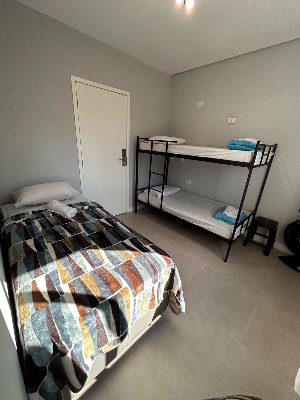 Quarto com beliche, cama de solteiro e porta.