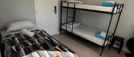 Quarto com beliche, cama de solteiro e porta.