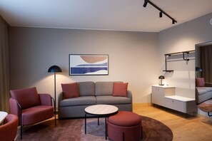Uma sala de estar moderna com um sofá cinza, poltronas vermelhas, uma mesa redonda pequena e um abajur.