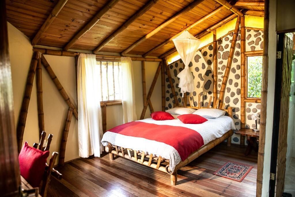 Quarto rústico com cama de madeira, janela com vista e teto de bambu.