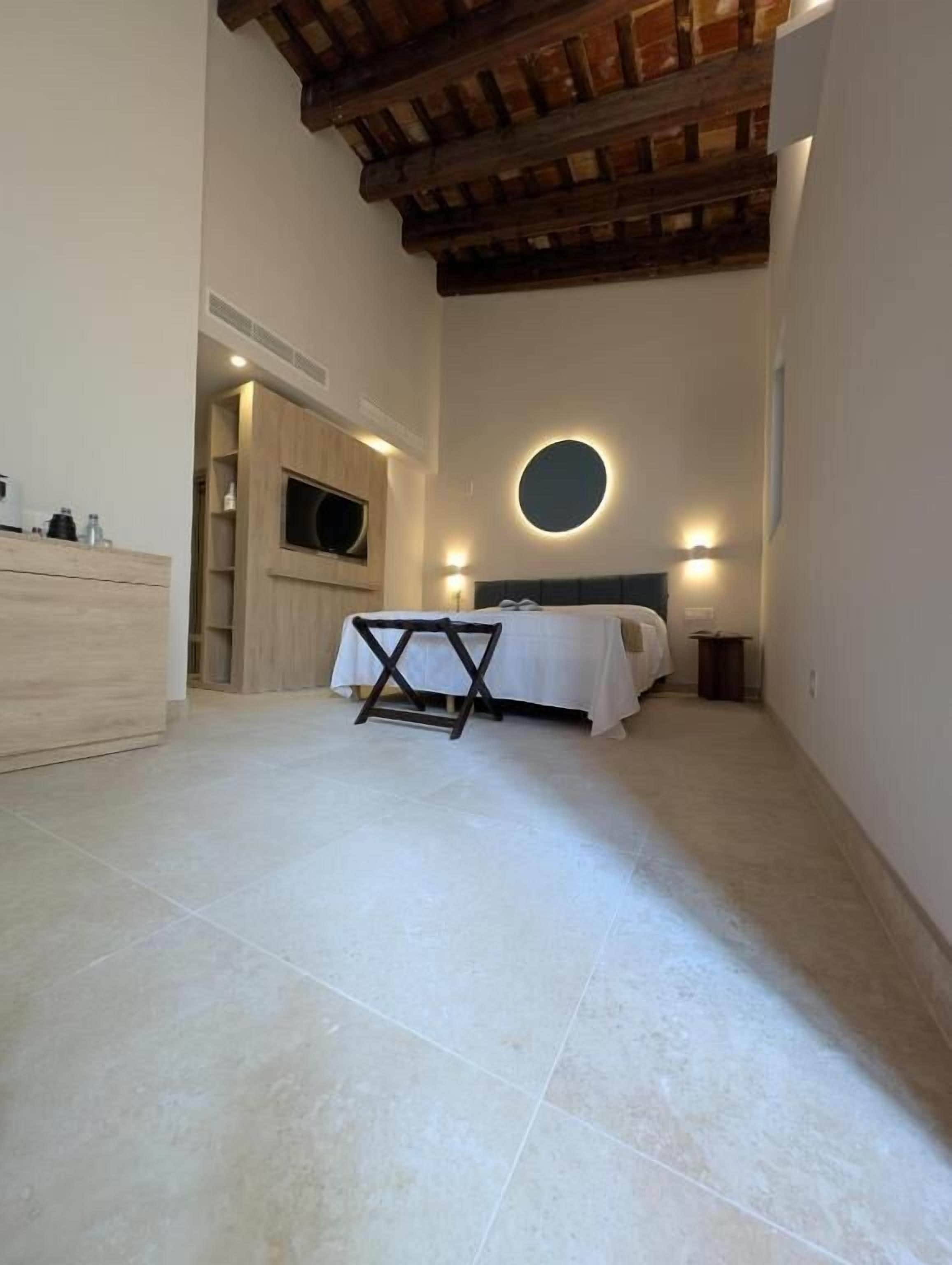 Quarto com cama, luminária redonda na parede, teto de madeira e piso em azulejo.