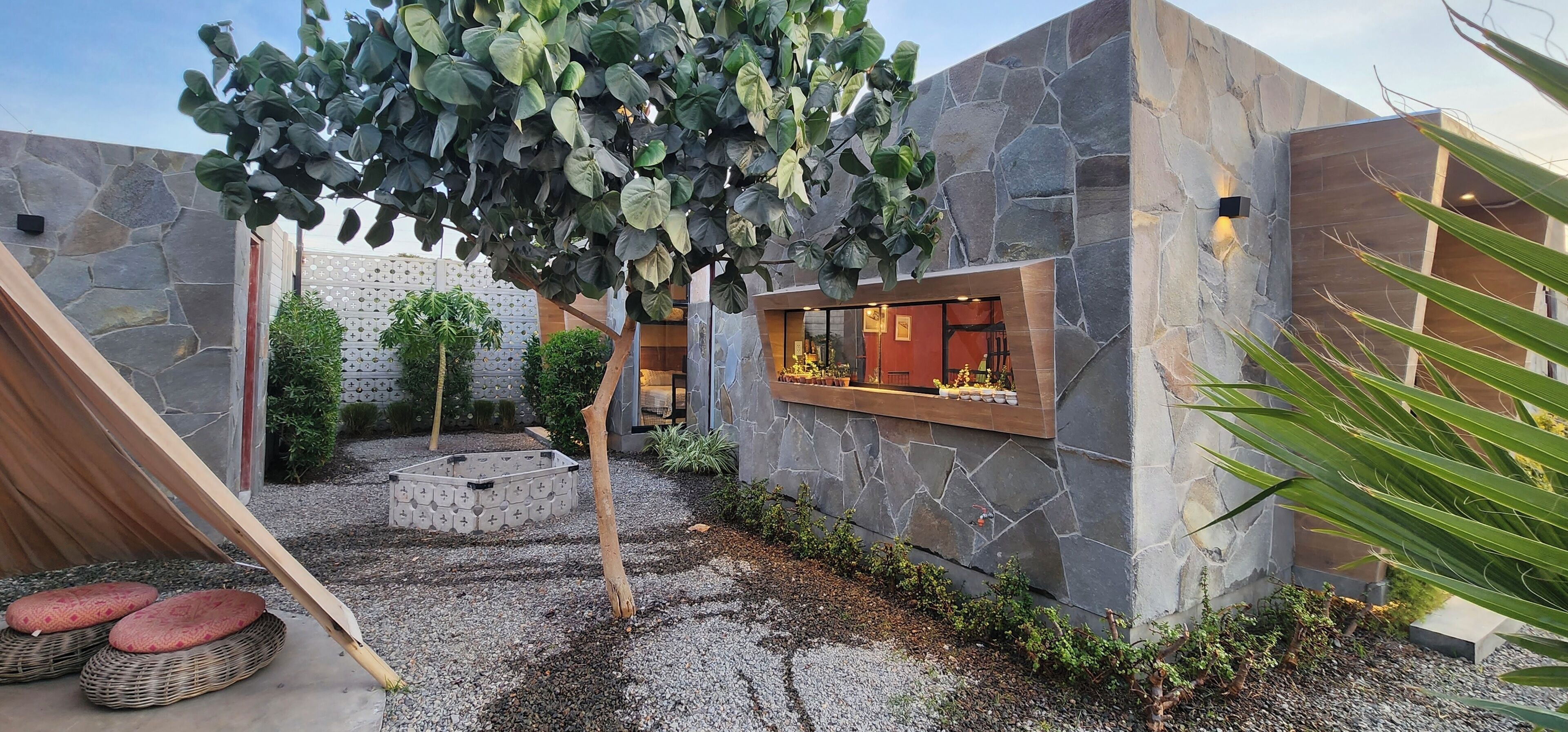 Uma área externa moderna com paredes de pedra, um banco de madeira e um pequeno jardim.