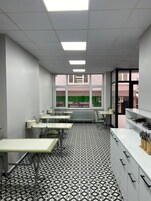 Uma cozinha com piso ladrilhado, armários brancos e uma janela com vista para um edifício.