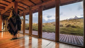 Quarto espaçoso com amplas janelas que oferecem vista para uma paisagem gramada e uma montanha nevada.