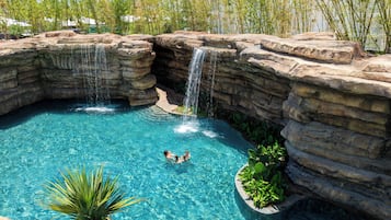 Piscina com cachoeira, cercada por formações rochosas e vegetação.
