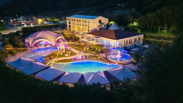 Um hotel com piscina, várias tendas e um edifício grande ao fundo.