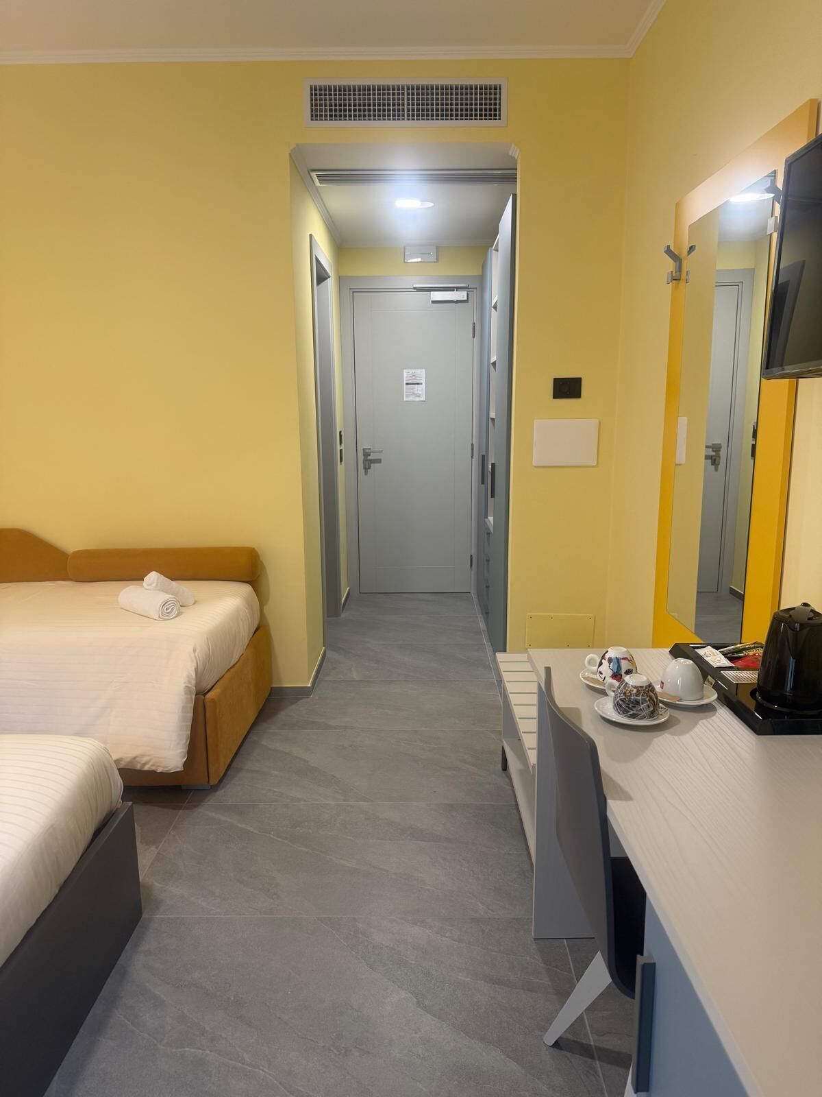 Quarto de hotel com cama, escrivaninha, cadeira, máquina de café e televisão.
