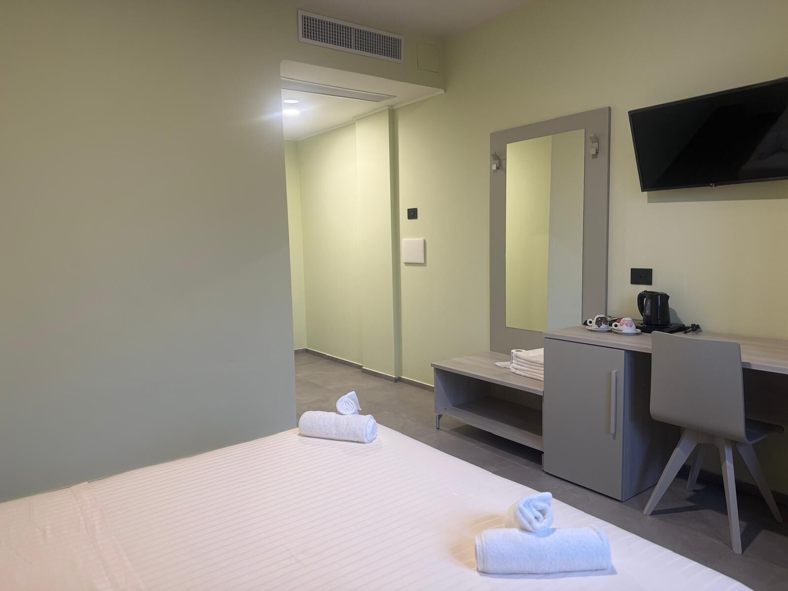 Quarto de hotel com cama, escrivaninha, cadeira, televisão e espelho.