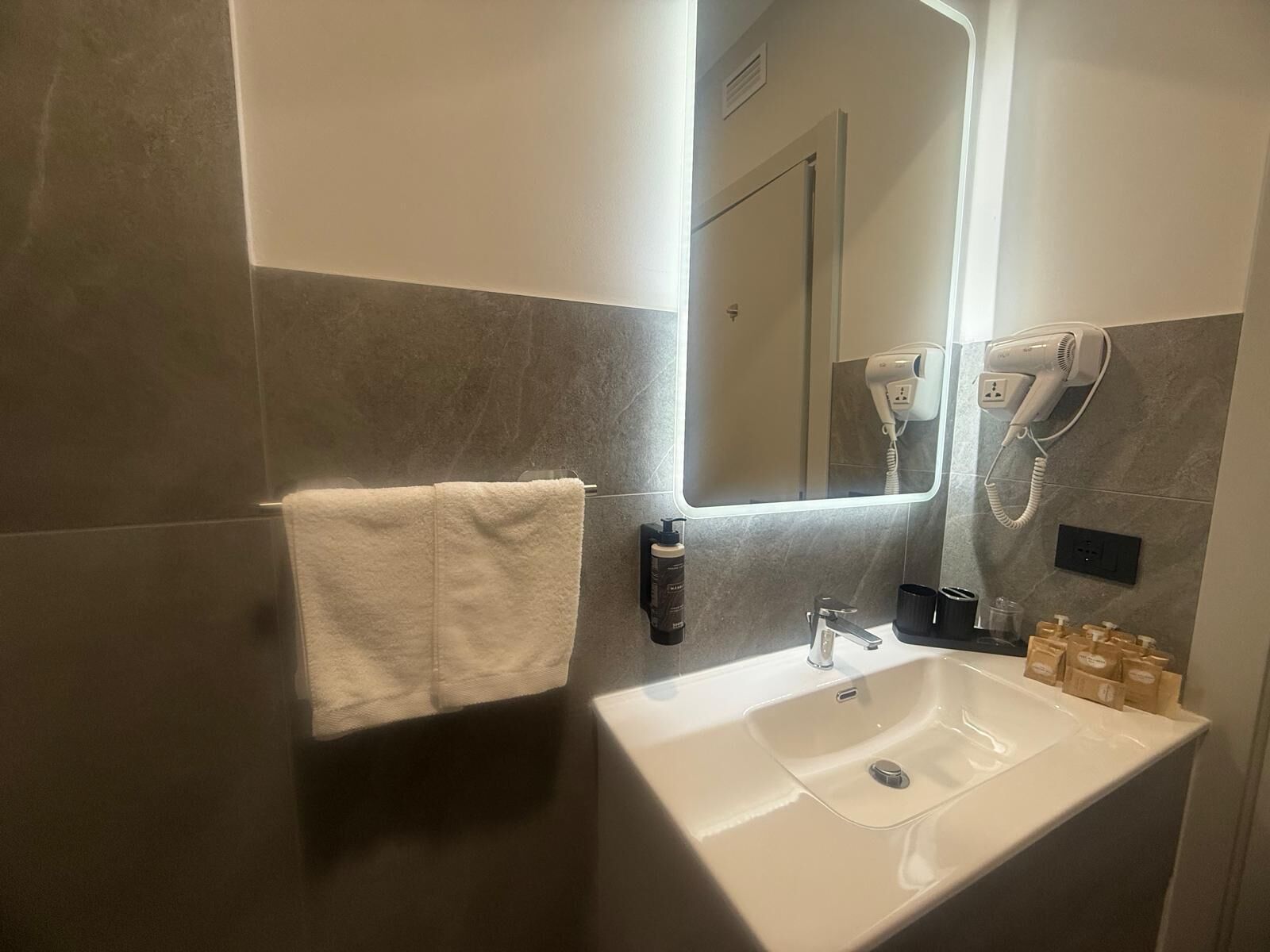 Casa de banho com lavatório, espelho, porta-toalhas, secador de cabelo e artigos de higiene pessoal.