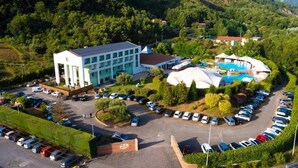Hotel com piscina, rodeado por vegetação exuberante e estacionamento.