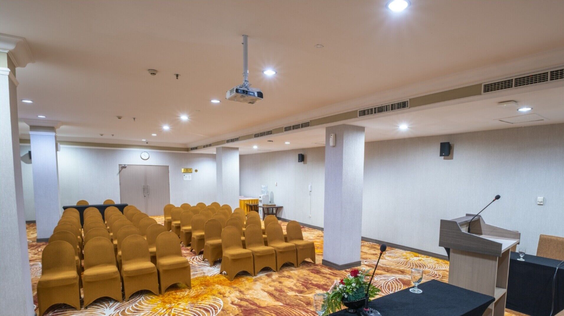Uma sala de conferências com fileiras de cadeiras, um púlpito e piso coberto por carpete.