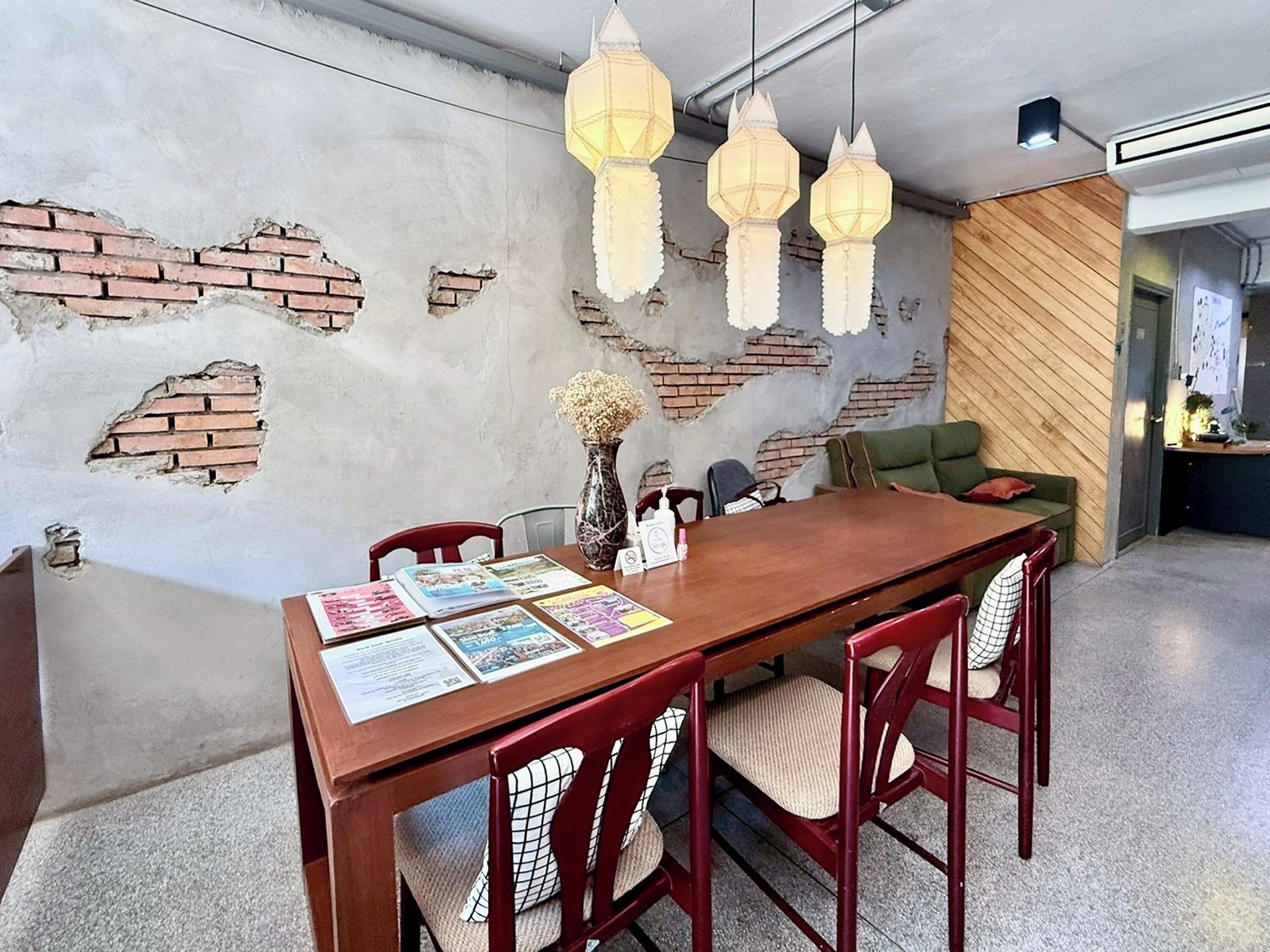 Uma área de refeições com uma mesa de madeira, cadeiras vermelhas, lanternas de papel penduradas e uma parede de tijolos aparentes.