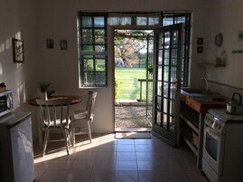 Cozinha com área de refeições, fogão e vista para um jardim através de portas abertas.