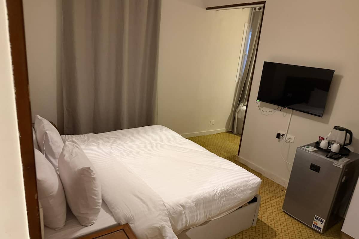 Quarto de hotel com uma cama, televisão fixada na parede e uma máquina de café.