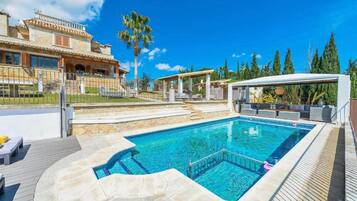 Uma piscina com um deck de madeira, cadeiras de sol e uma área de estar coberta.
