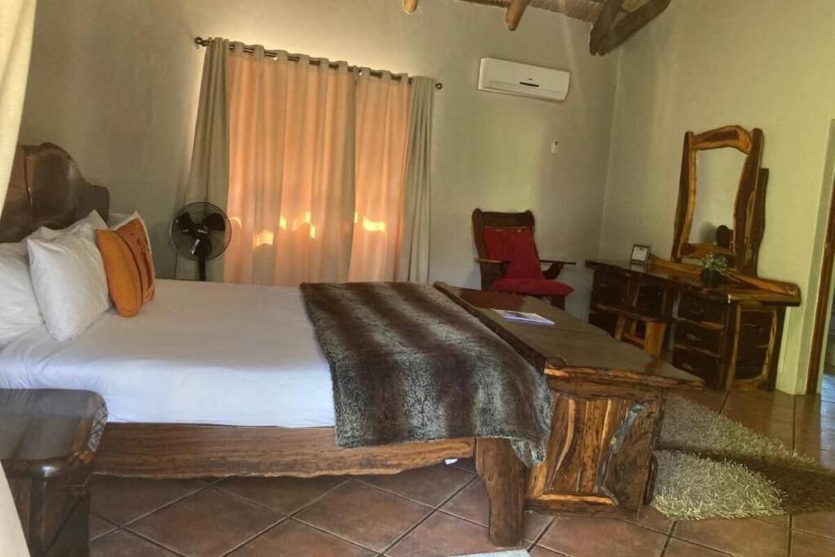 Quarto com uma cama grande, um banco de madeira, uma escrivaninha, uma cadeira e um espelho.