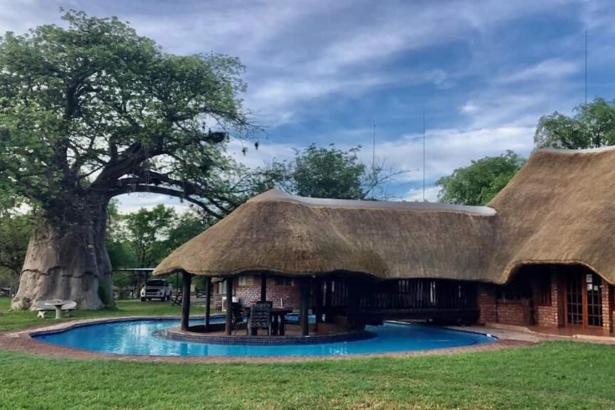 Um edifício com telhado de palha e piscina em frente.