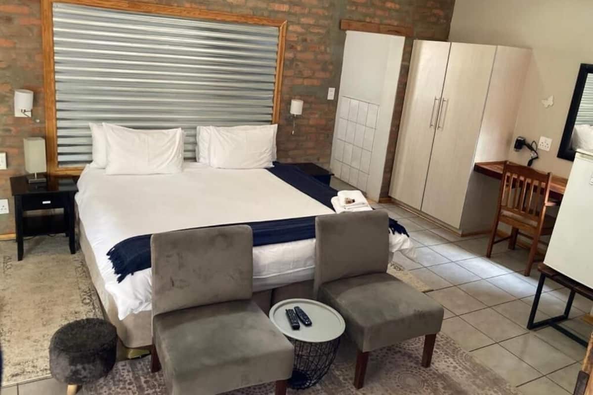 Quarto de hotel com uma cama grande, duas cadeiras, uma mesa redonda pequena, um guarda-roupa e uma escrivaninha com cadeira.