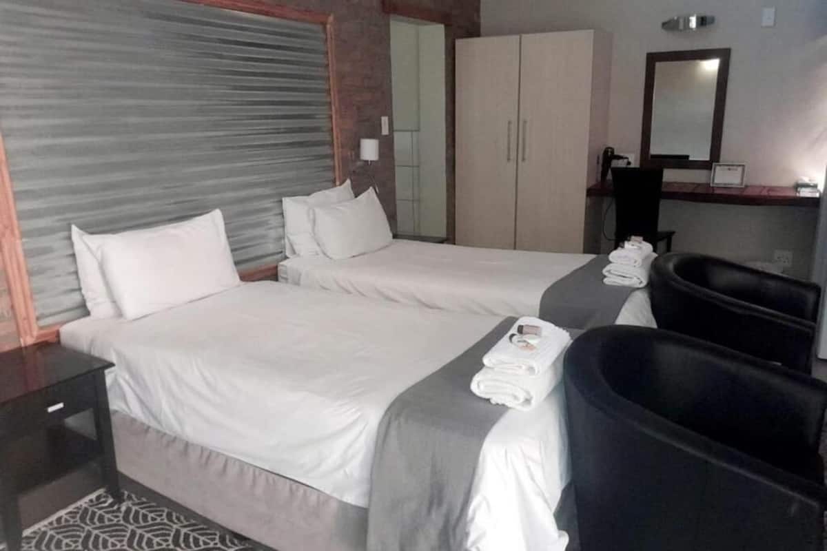 Quarto de hotel com duas camas, um espelho grande, um guarda-roupa e uma banheira preta.