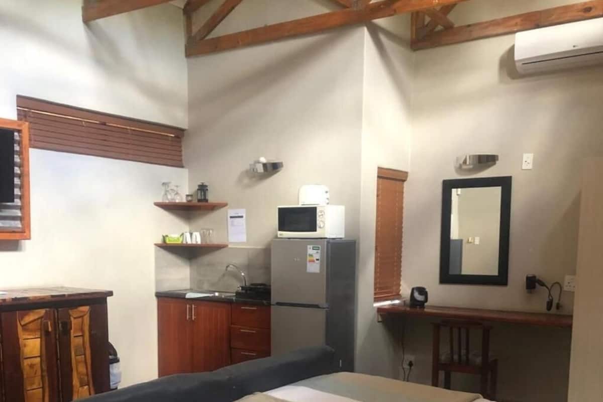 Quarto compacto com cama, cozinha compacta equipada com micro-ondas e geladeira, armário de madeira e espelho na parede.
