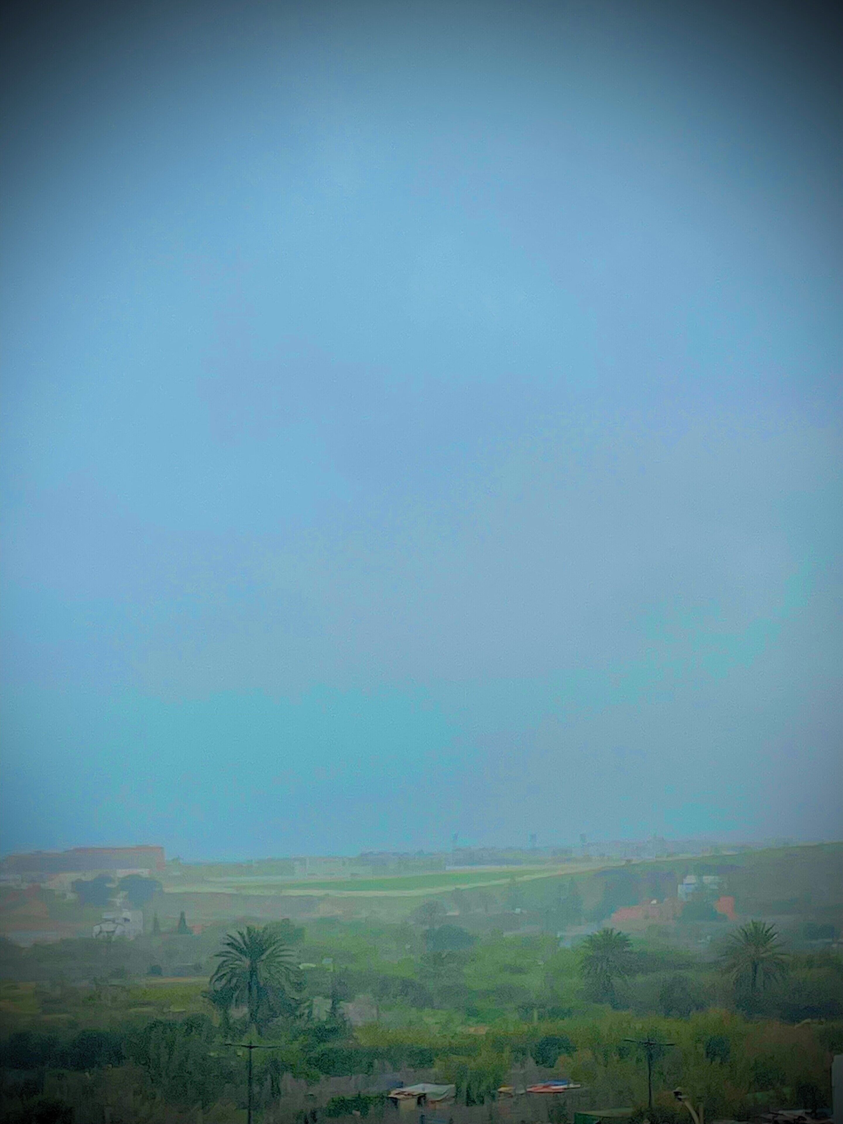 Paisagem rural com céu claro, campos verdes e edifícios dispersos.