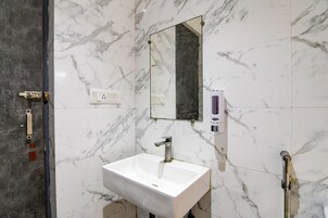 Casa de banho com lavatório de mármore, espelho, chuveiro manual e dispensador de toalhas.