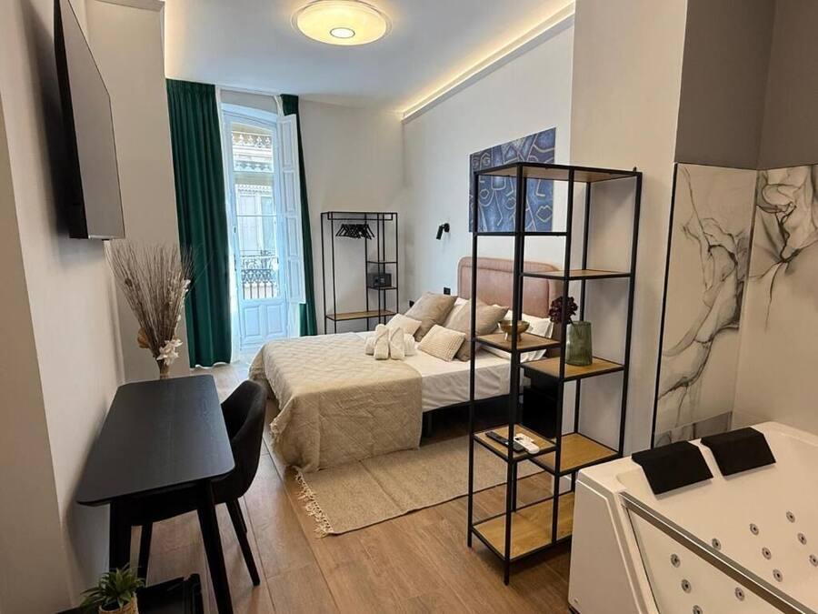 Quarto de hotel moderno com cama, escrivaninha, cadeira, guarda-roupa e banheiro.