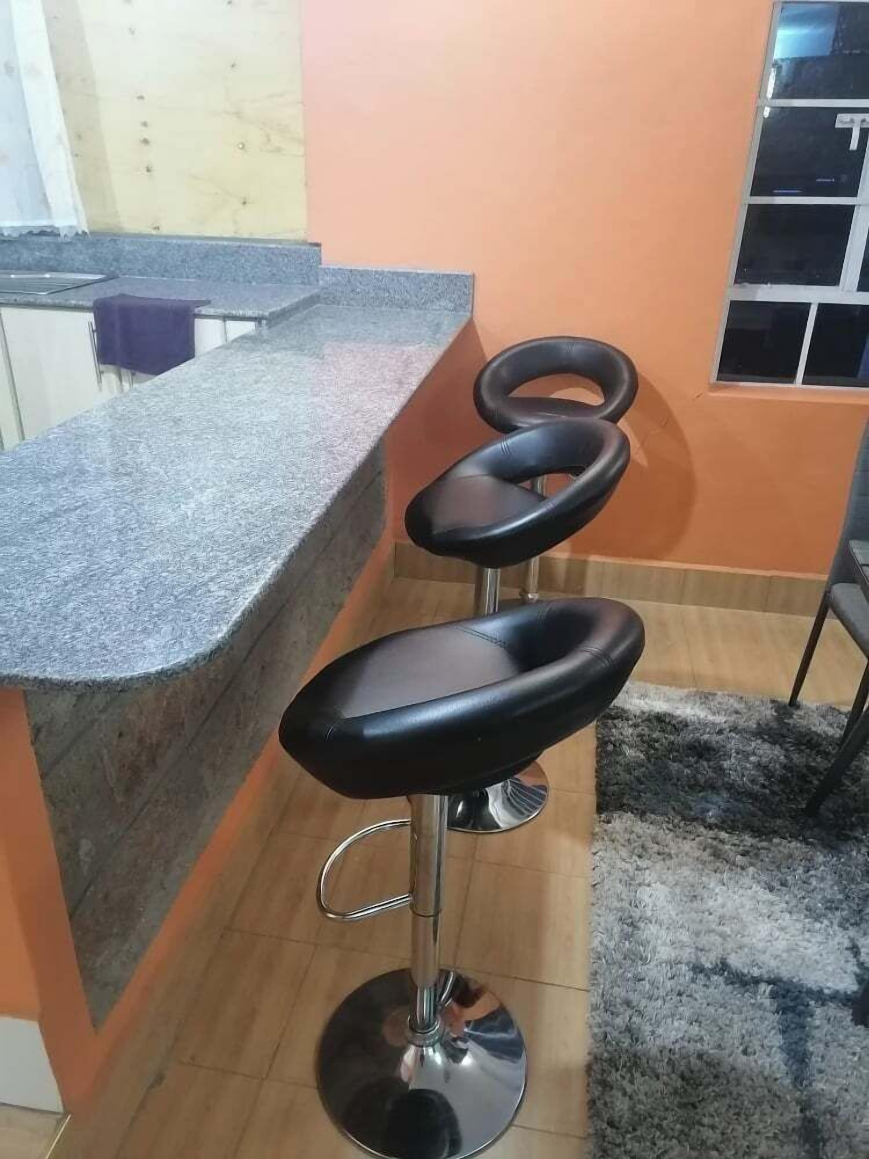 Uma cozinha com bancada de granito, pia e um banquinho de barra com assento preto e base de metal.