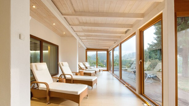 Um quarto banhado por luz solar, com poltronas de vime e amplas janelas que oferecem vista para o exterior.