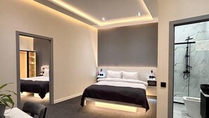 Quarto de hotel moderno com uma cama grande, mesas de cabeceira, uma escrivaninha e área de chuveiro.
