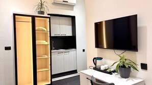 Quarto moderno com escrivaninha, televisão na parede, cozinha planejada e armário com prateleiras iluminadas.
