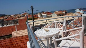 Terraço no telhado com uma mesa redonda e cadeiras, com vista para uma cidade costeira com edifícios de telhado vermelho.