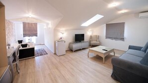 Uma sala de estar moderna e bem iluminada, com uma TV de tela plana, um sofá, uma mesa de centro e um espaço de jantar com uma mesa e cadeiras.