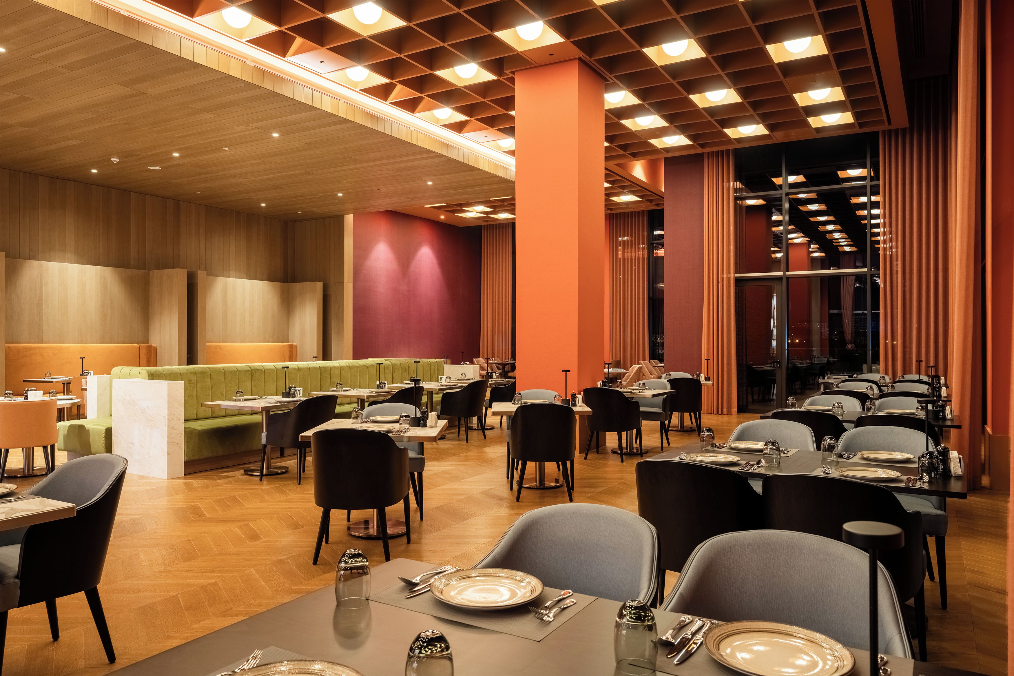 Um restaurante moderno com diversas opções de assento, incluindo cabines e mesas, teto de madeira com iluminação embutida e uma paleta de cores quentes.