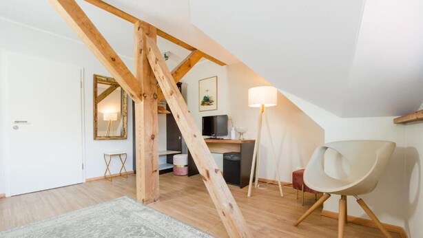 Quarto em estilo loft com vigas de madeira aparentes, uma escrivaninha, uma cadeira e um abajur.