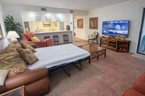 Uma sala de estar com cama, sofá, televisão, mesa pequena e espaço para bar.