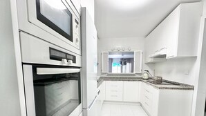 Uma cozinha moderna com armários brancos, forno embutido e bancada de granito.