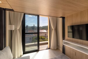 Quarto moderno com uma televisão grande, portas de vidro deslizantes para uma varanda e um sofá.