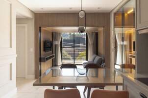 Uma zona de refeições moderna com uma mesa de vidro, cadeiras, uma televisão e vista para o exterior.