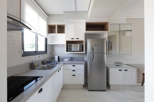 Uma cozinha moderna com armários brancos, uma geladeira de aço inoxidável, micro-ondas e uma placa de indução.