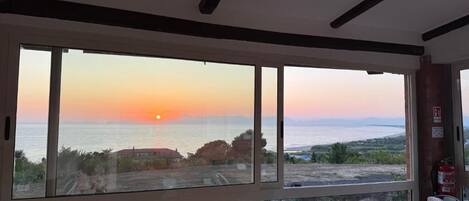 Quarto com uma grande janela com vista para um pôr do sol sobre o mar.