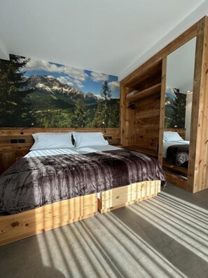 Quarto com cama, cabeceira de madeira e um mural de paisagem montanhosa.