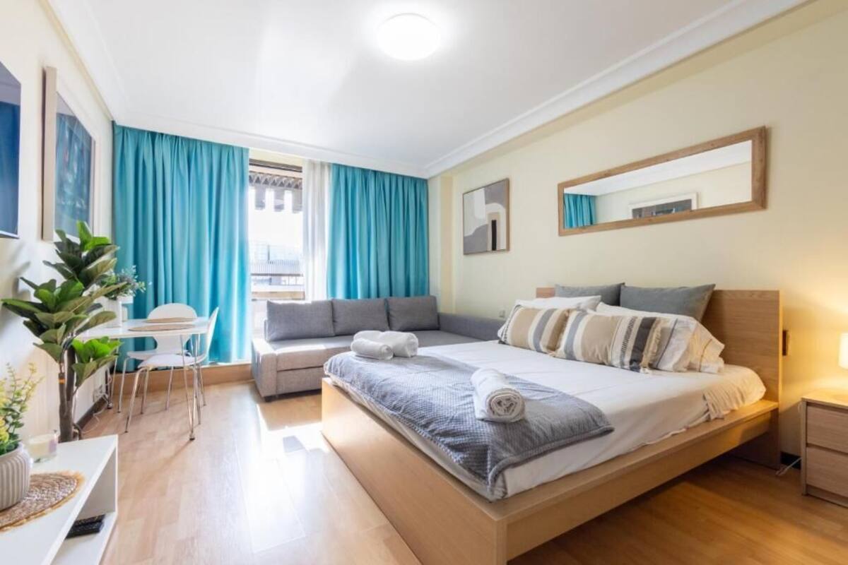 Quarto moderno com cama grande, sofá, área de jantar e vista para a cidade.