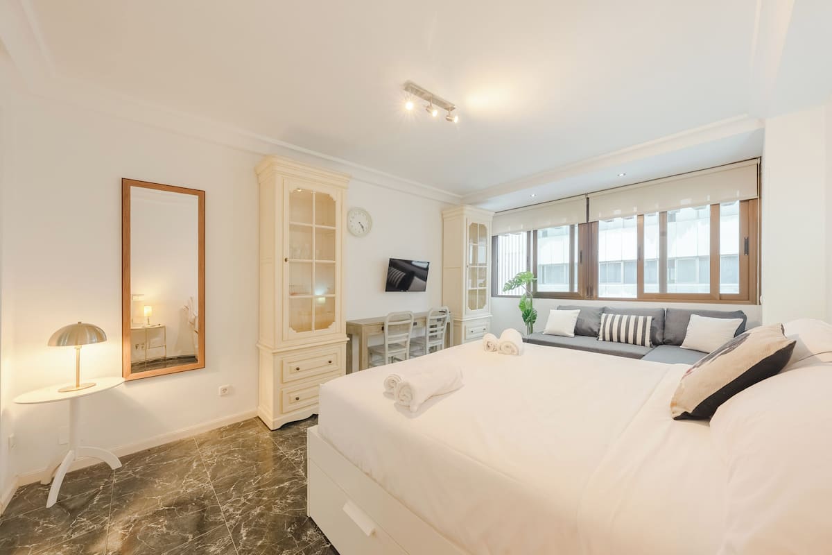 Quarto de hotel com cama, escrivaninha, cadeira, armário, televisão e janela com vista.
